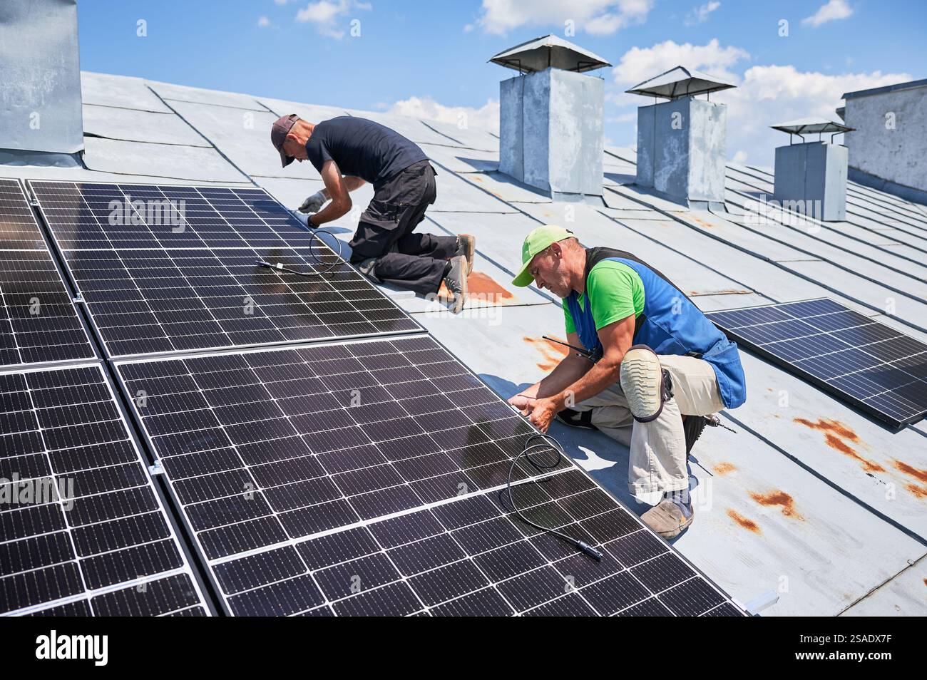 Workers building solar panel system on metal rooftop of house. Two men installers installing ...