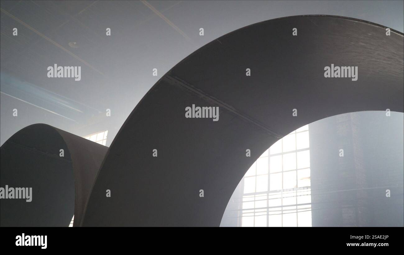 Sunlight illuminates large steel pipes bending in an industrial ...