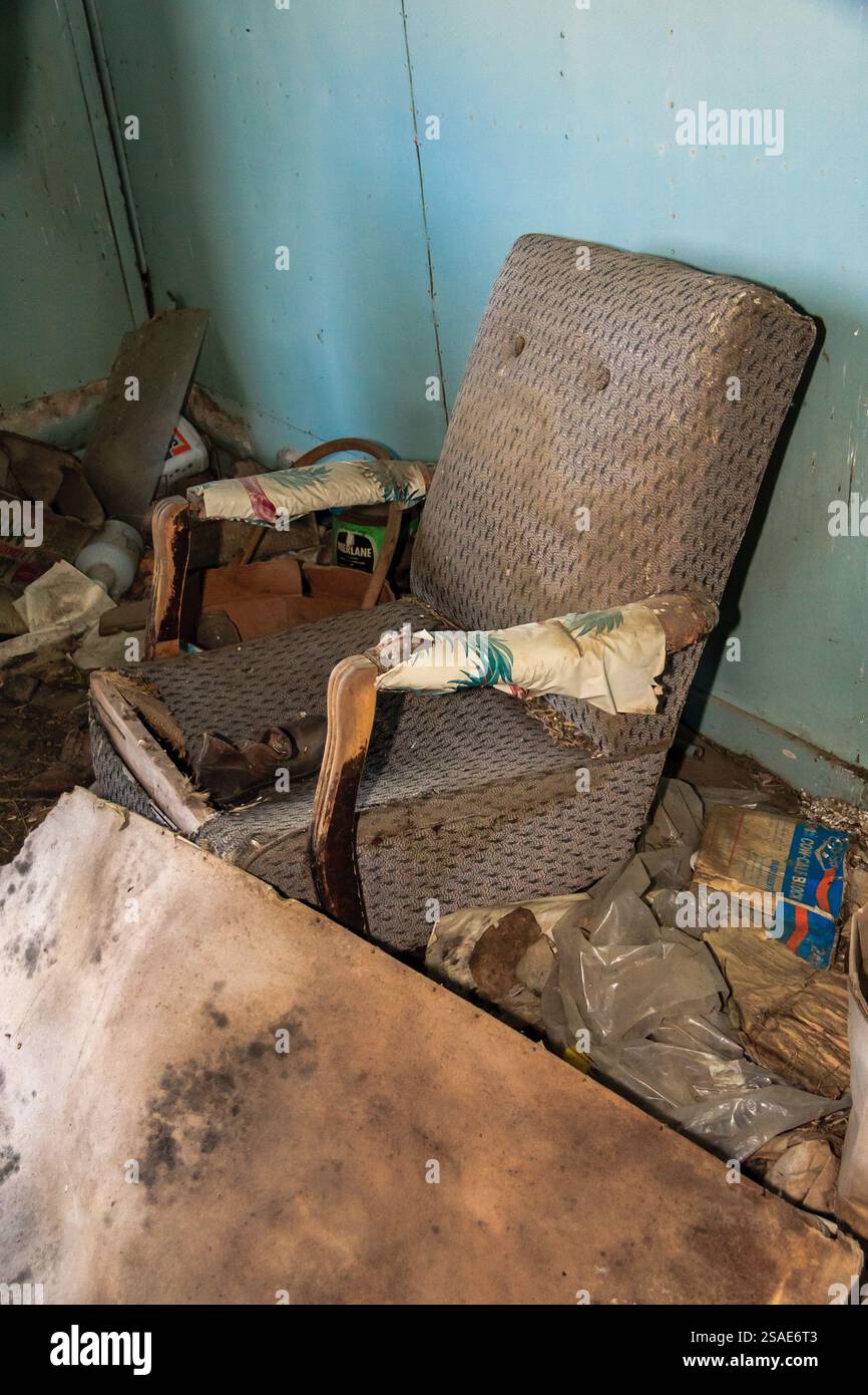 A chair is sitting on the floor in a messy room. The chair is old and ...