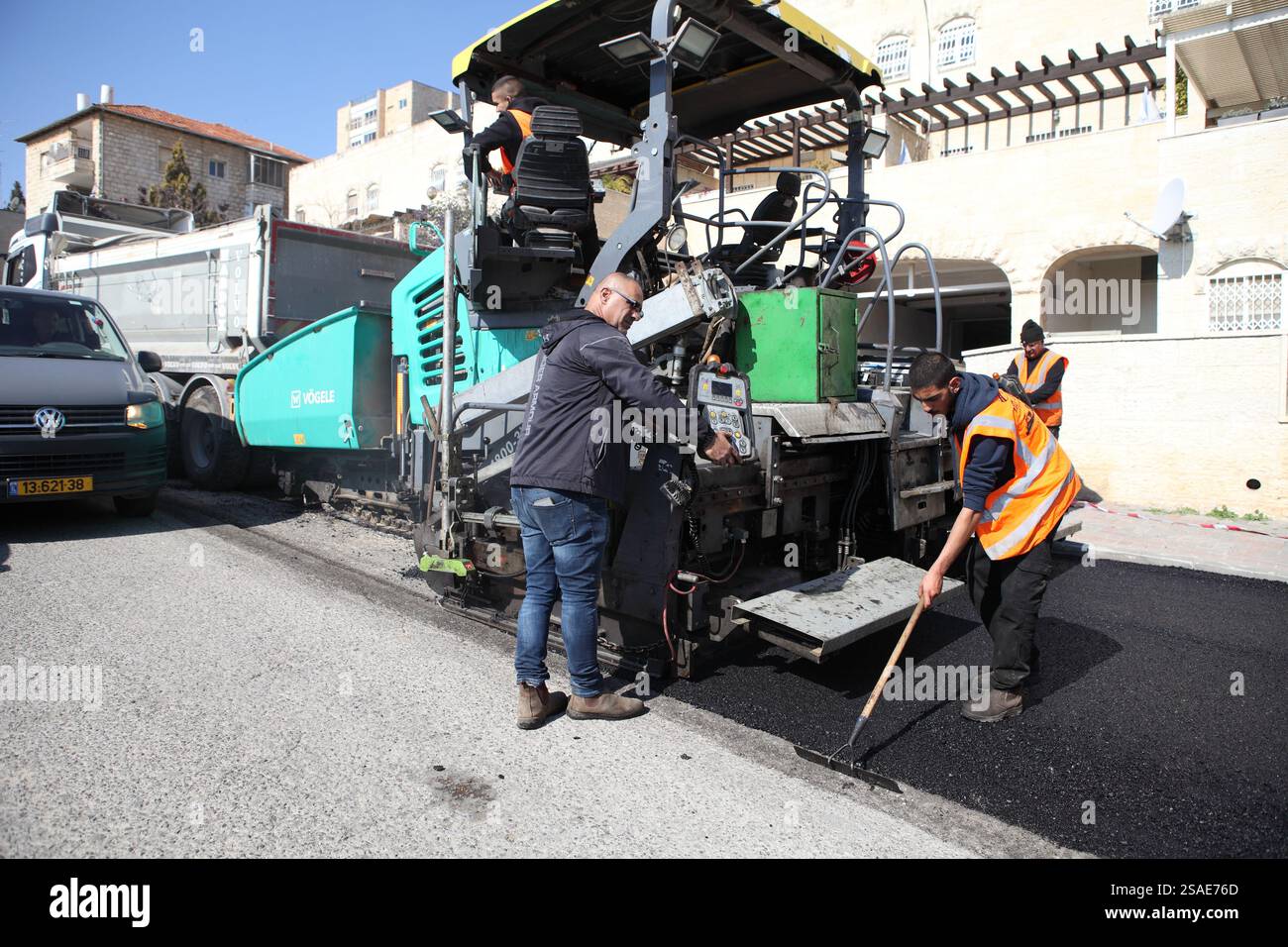 Palestinian worker wearing protective vest spreads asphalt poured by ...