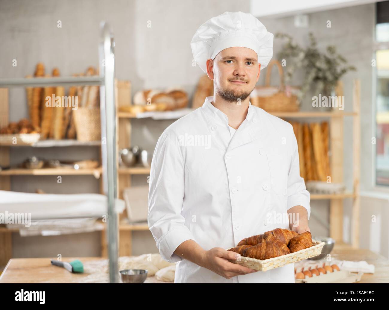 Baker in white uniform stands behind counter in small private bakery ...