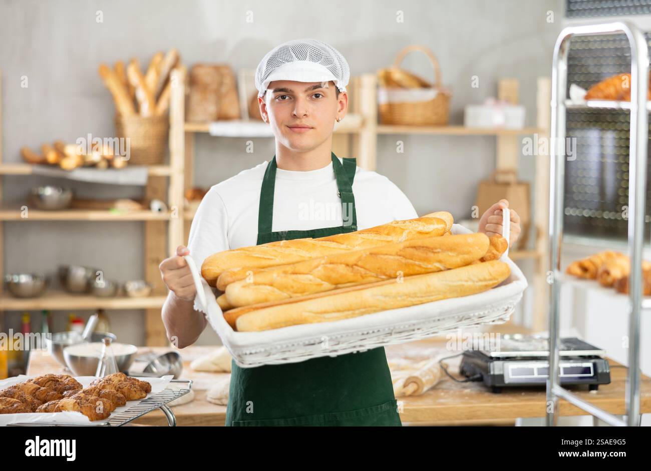 Happy male baker posing with basket of freshly baked baguettes in ...