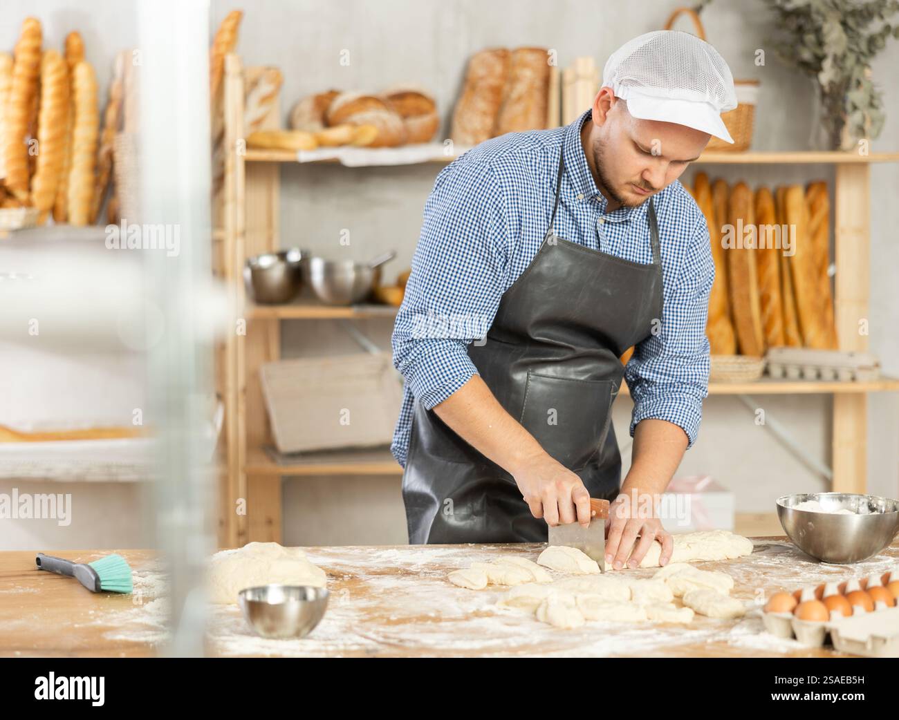 Guy works in bakery as baker, cuts dough into portions, forms pieces of ...