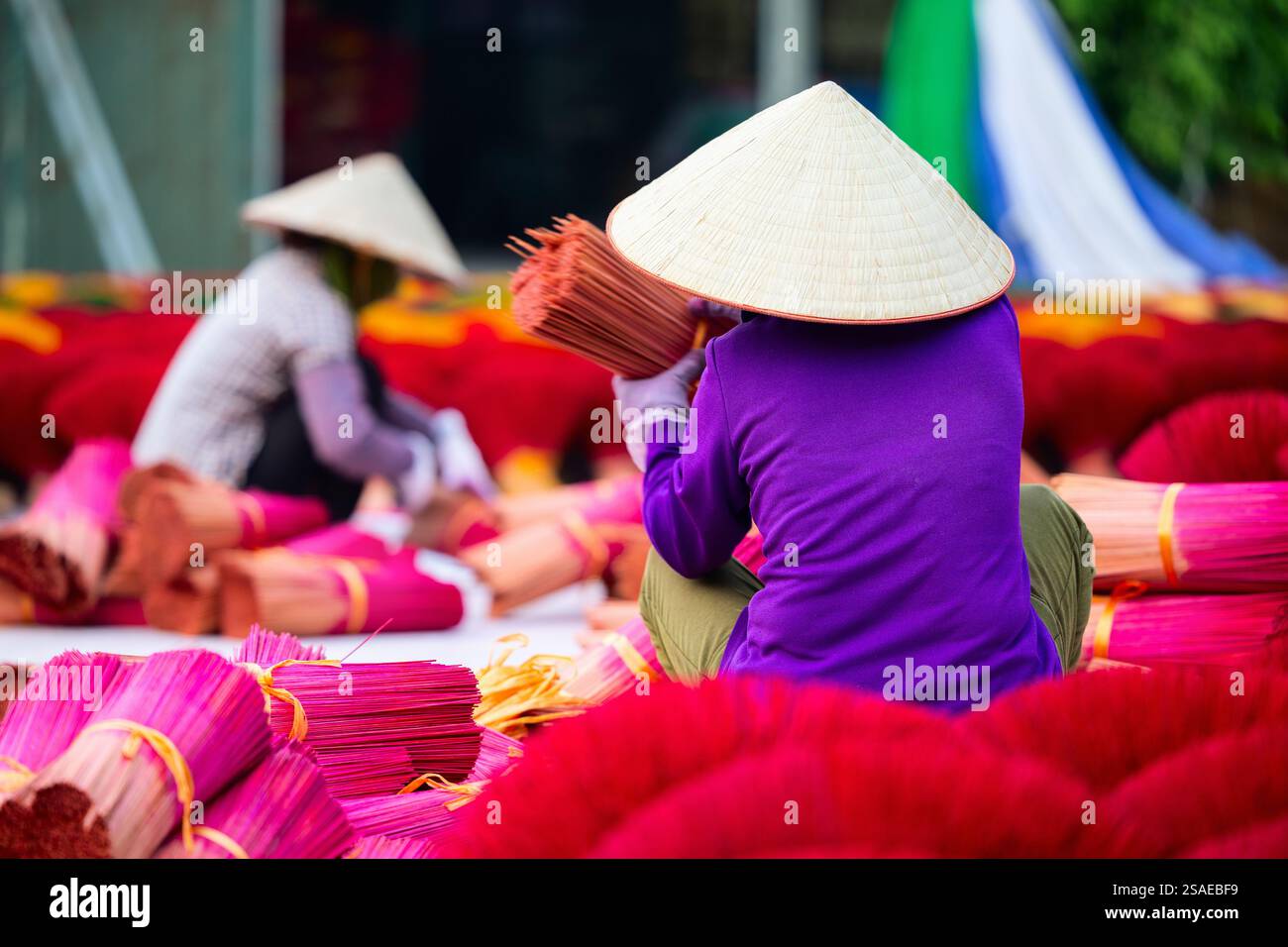 Two woman workers wearing conical hats among red incense sticks drying ...