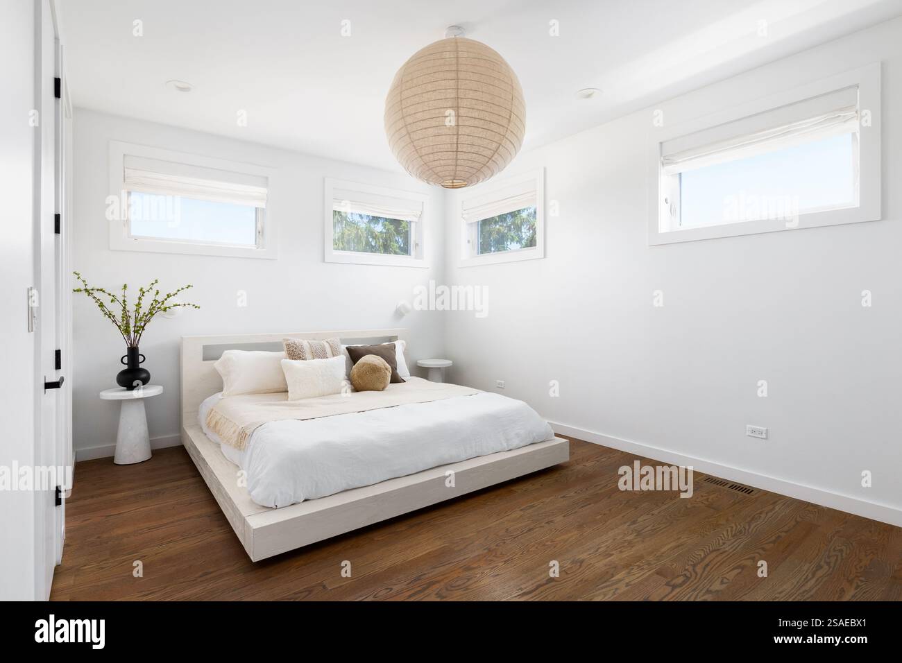 A minimalistic bedroom with dark hardwood flooring, a short bed with ...