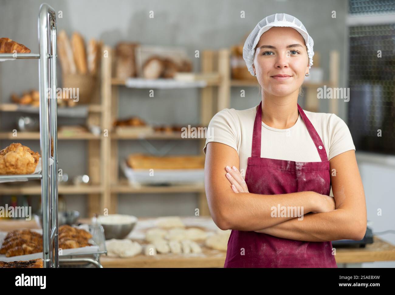 Successful young female baker posing with arms crossed in bakery Stock ...