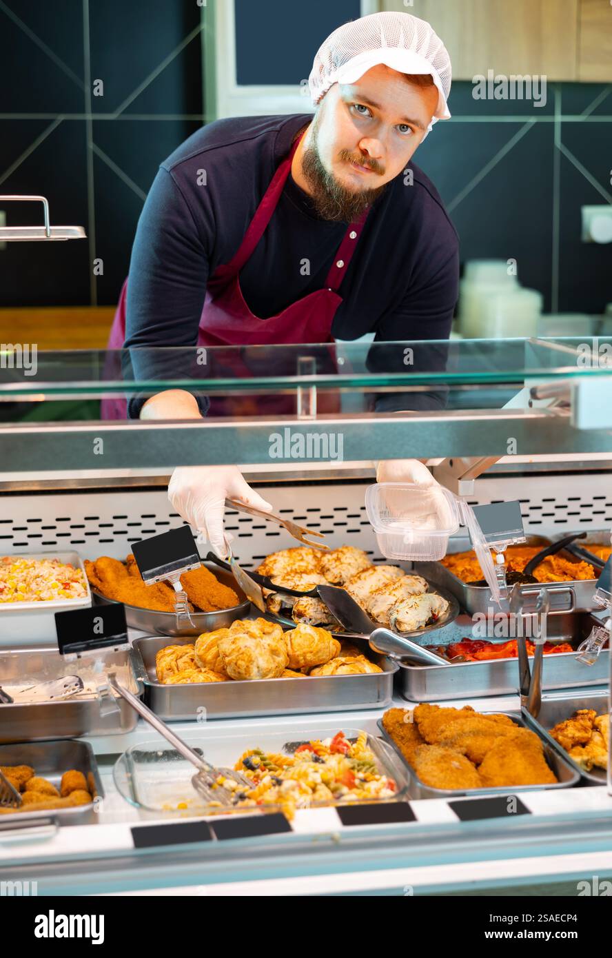 Salesman serving ready-to-eat dishes from deli counter in supermarket ...