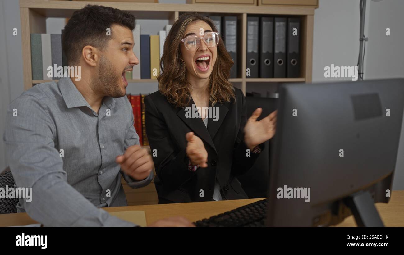 Man and woman cheering together in an office setting while looking at a ...