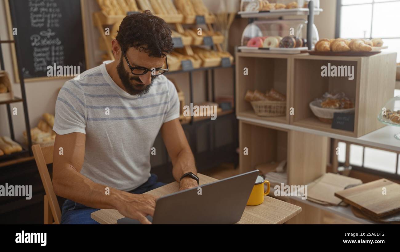Young hispanic man with beard working on laptop in a cozy bakery shop ...