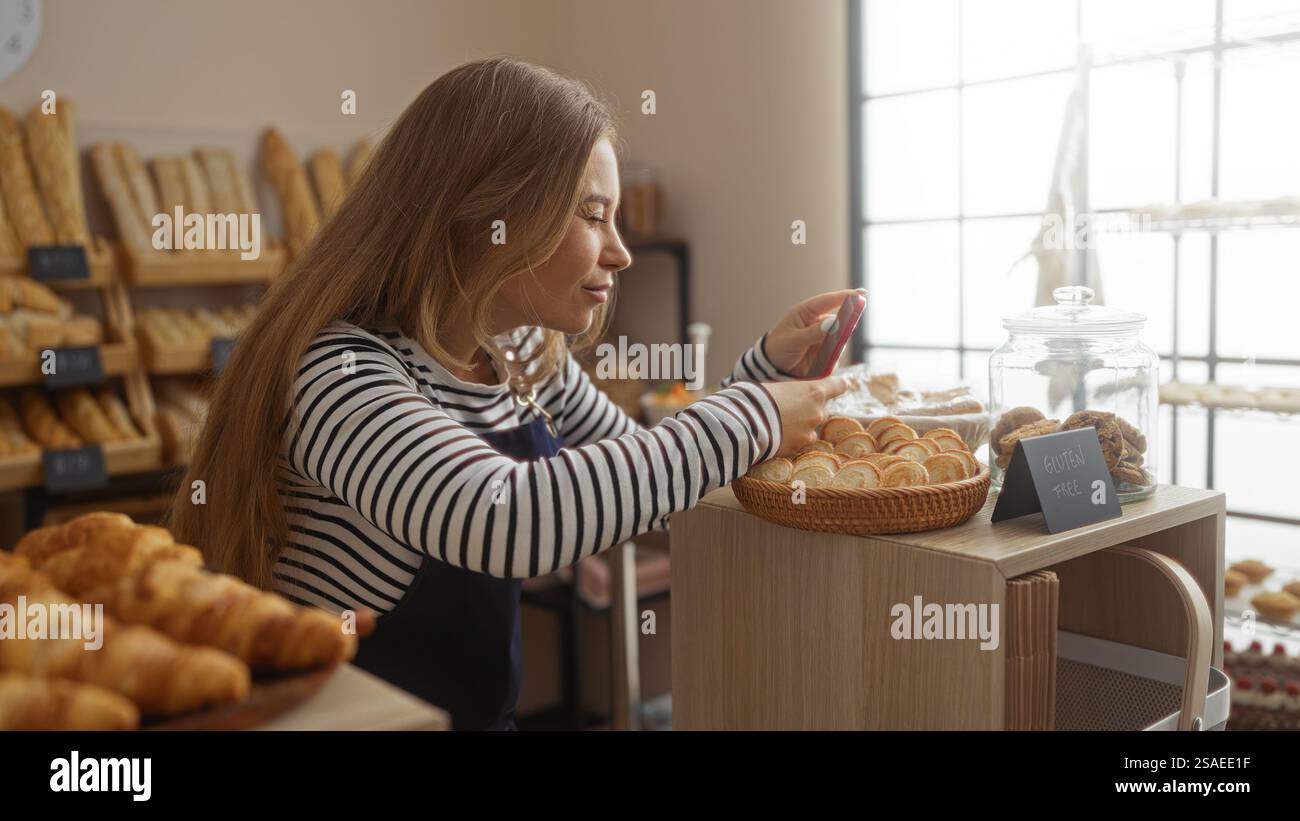 Young blonde woman working indoors at a bakery photographing pastries ...