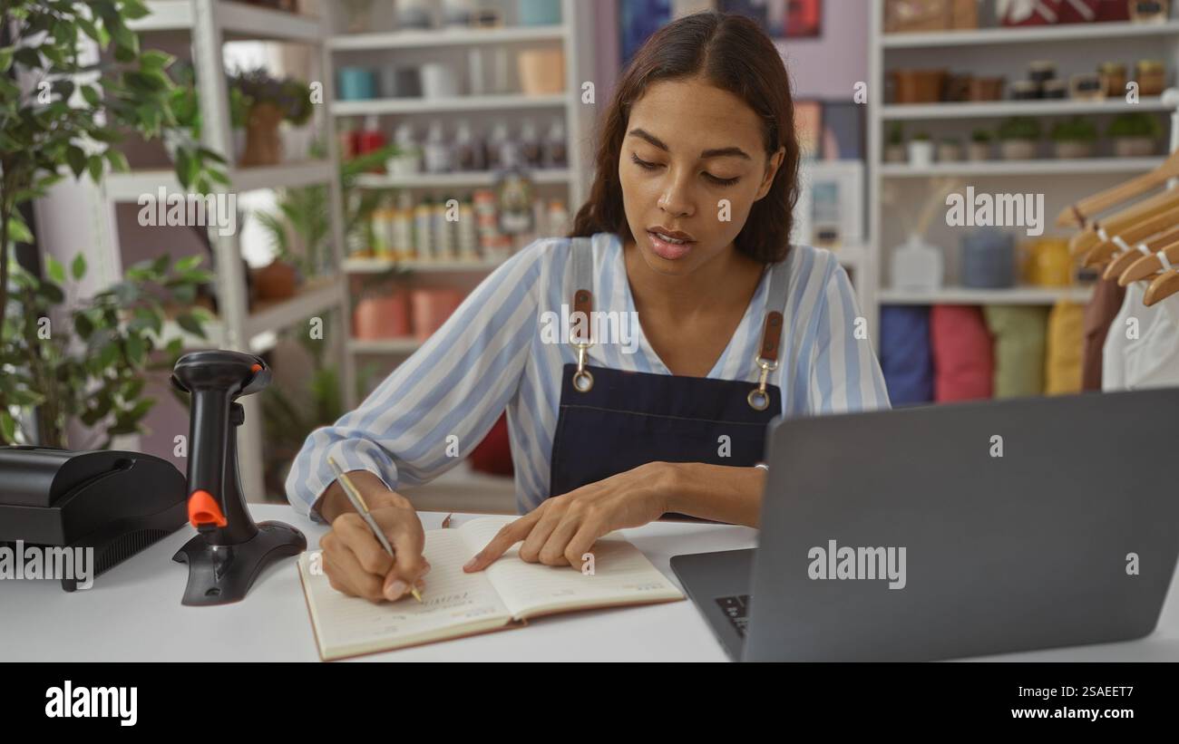 Young woman working in a home decor store taking notes with a laptop ...