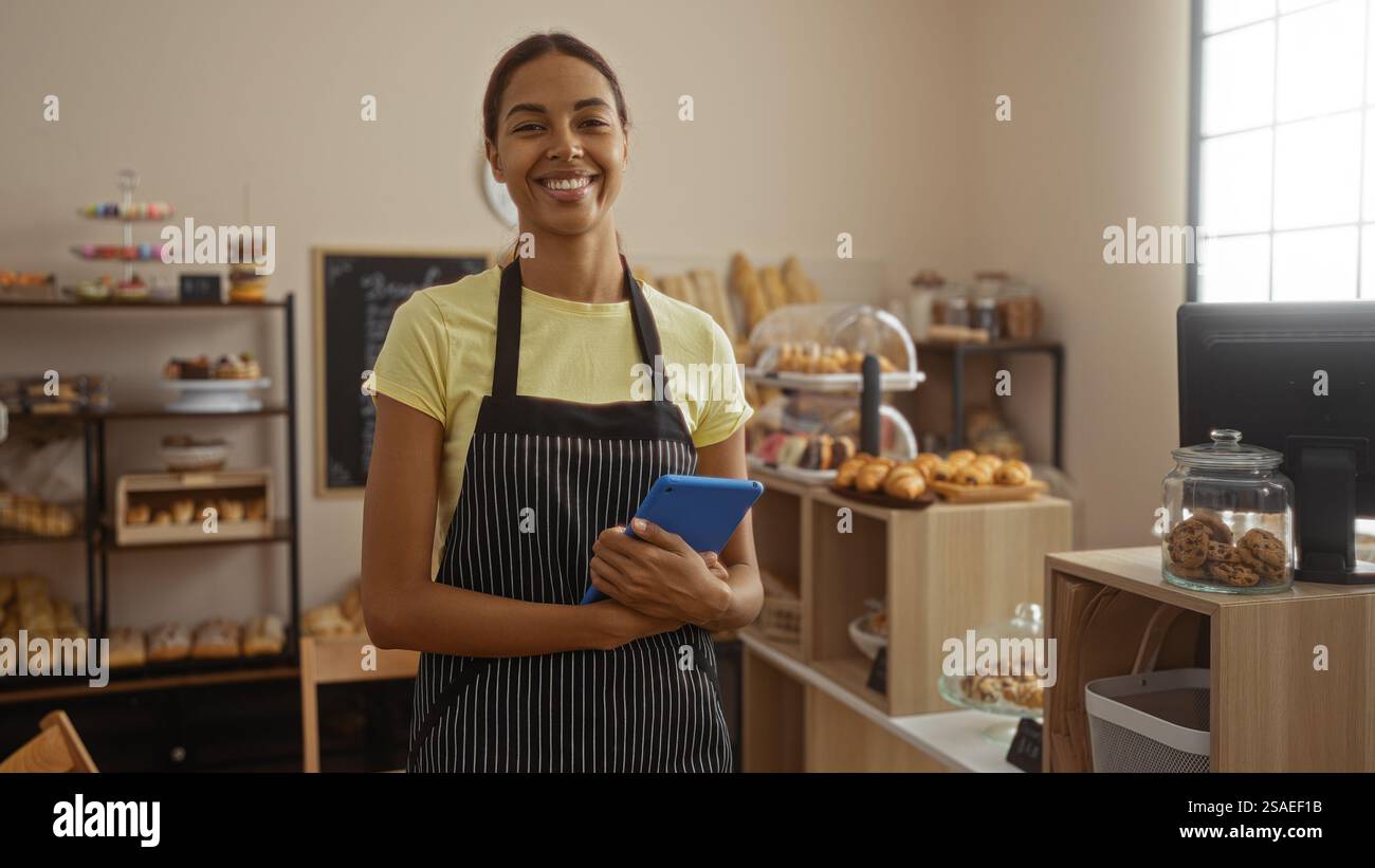 Woman smiling inside a bakery holding a tablet, surrounded by various ...
