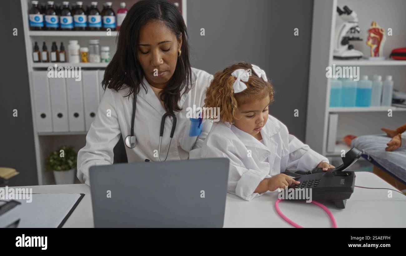 Woman doctor with girl in clinic room working on laptop and phone ...