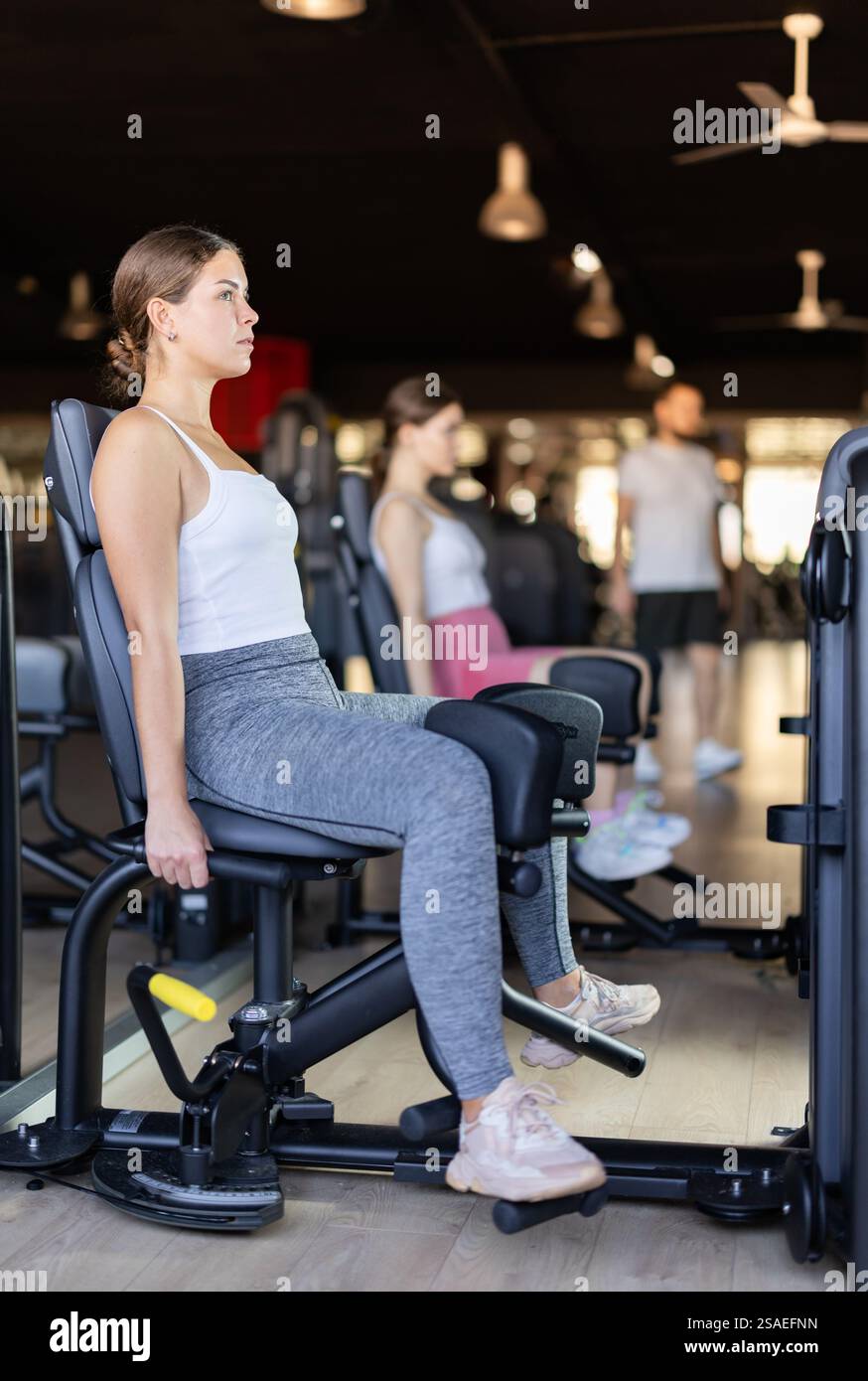 Slender athletic girl work out muscles of legs and thighs on simulator ...
