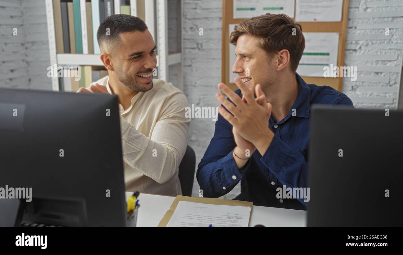 Handsome men working indoors clapping at computers signifying teamwork ...