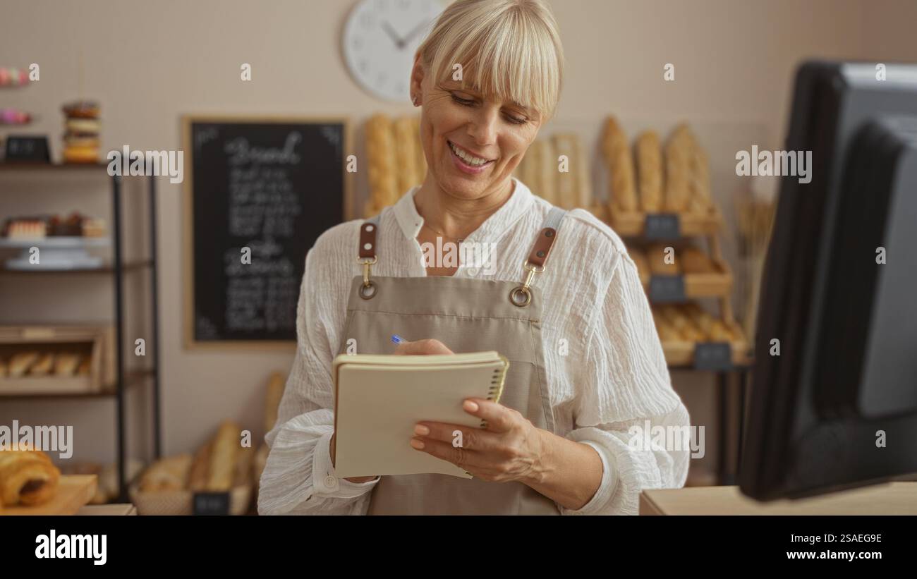 Woman smiling while writing in a notebook at a bakery shop counter with ...