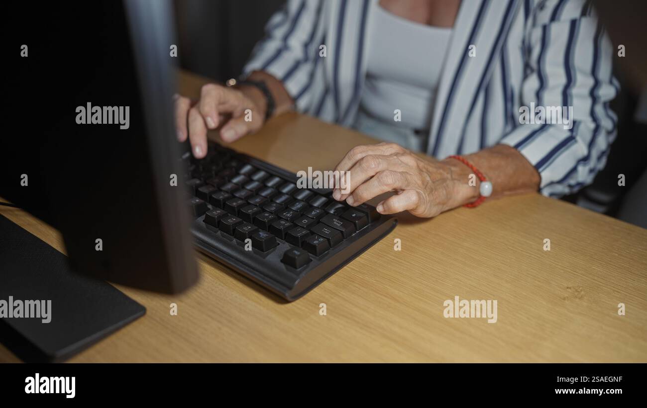 Mature woman typing on a keyboard in an office setting, wearing a ...