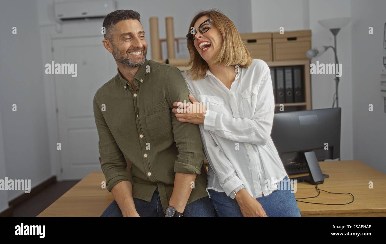 Man and woman laughing together in a modern office, indicating a ...