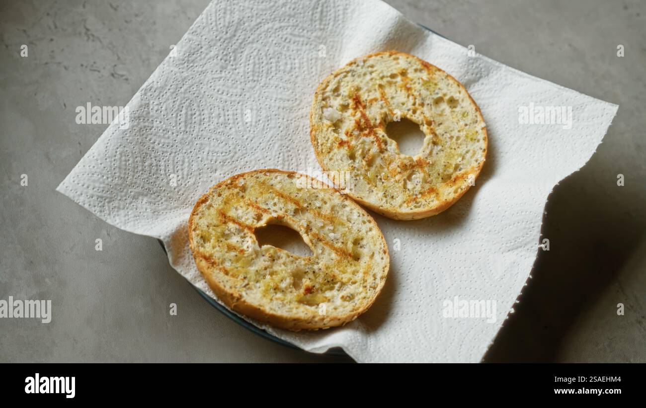 Toasted bagel halves sitting on a paper towel over a concrete surface ...