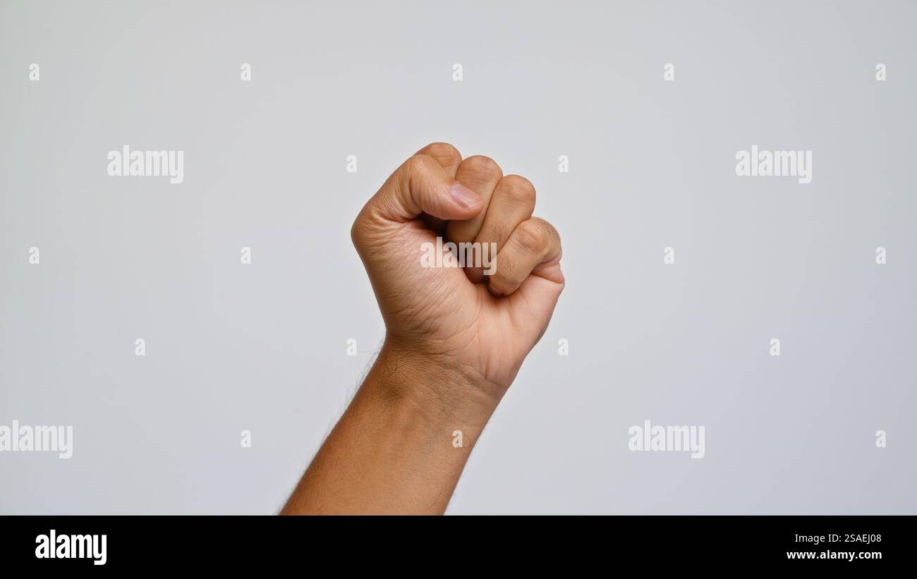 Man holding clenched fist against plain white background symbolizing ...
