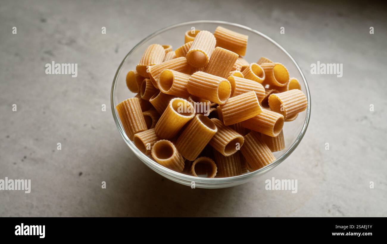Uncooked pasta arranged neatly in a clear glass bowl against a textured ...