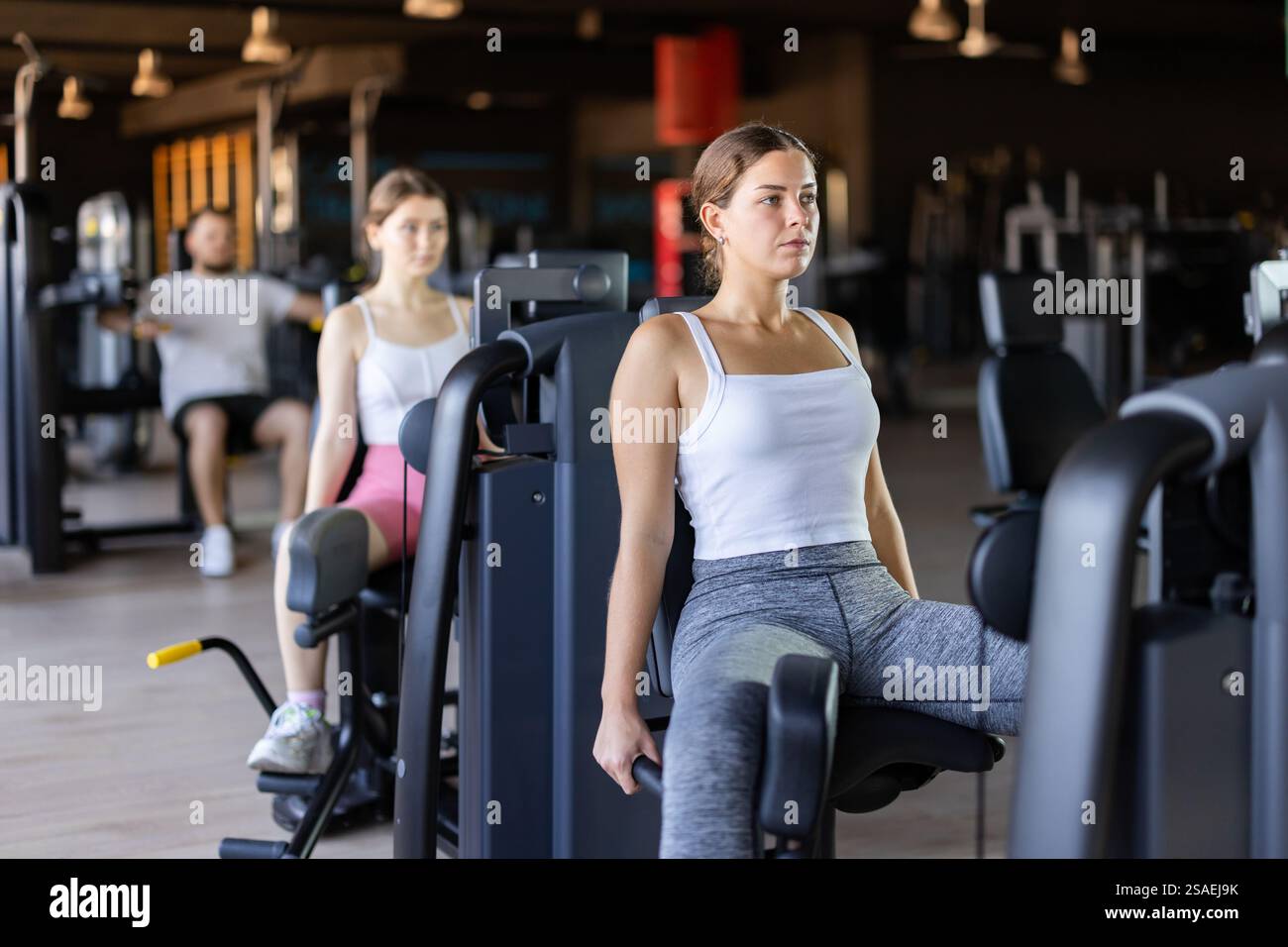 Slender athletic girl work out muscles of legs and thighs on simulator ...