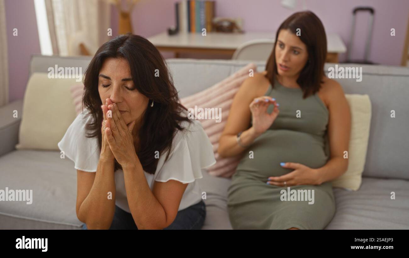 Pregnant woman discussing with mother sitting on couch at home ...