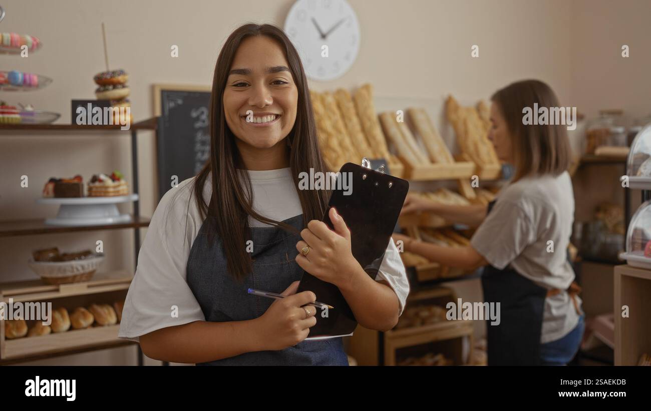 Two women workers in a bakery, one smiling with a clipboard and the ...