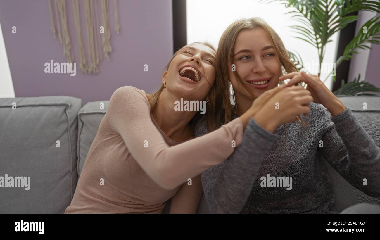 Sisters laughing together on a cozy sofa in a bright living room, capturing the warmth and love ...