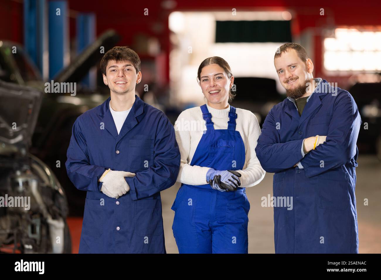 Team of auto mechanics, two men and one woman, wearing blue overalls ...