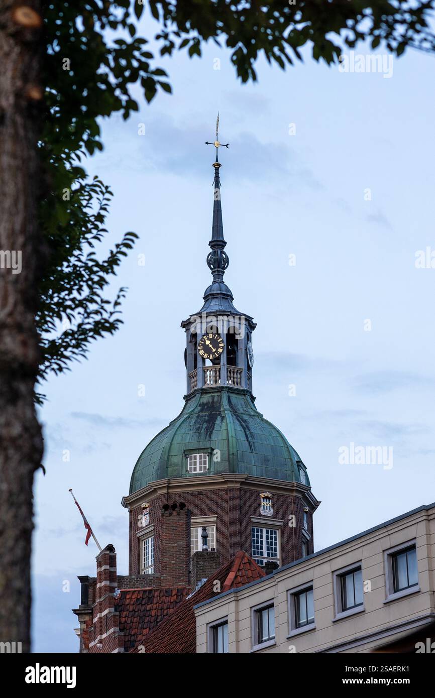 A historic clock tower with a green dome and spire rises above brick ...