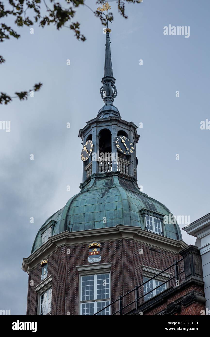 A historic clock tower with a green dome and spire rises above brick ...