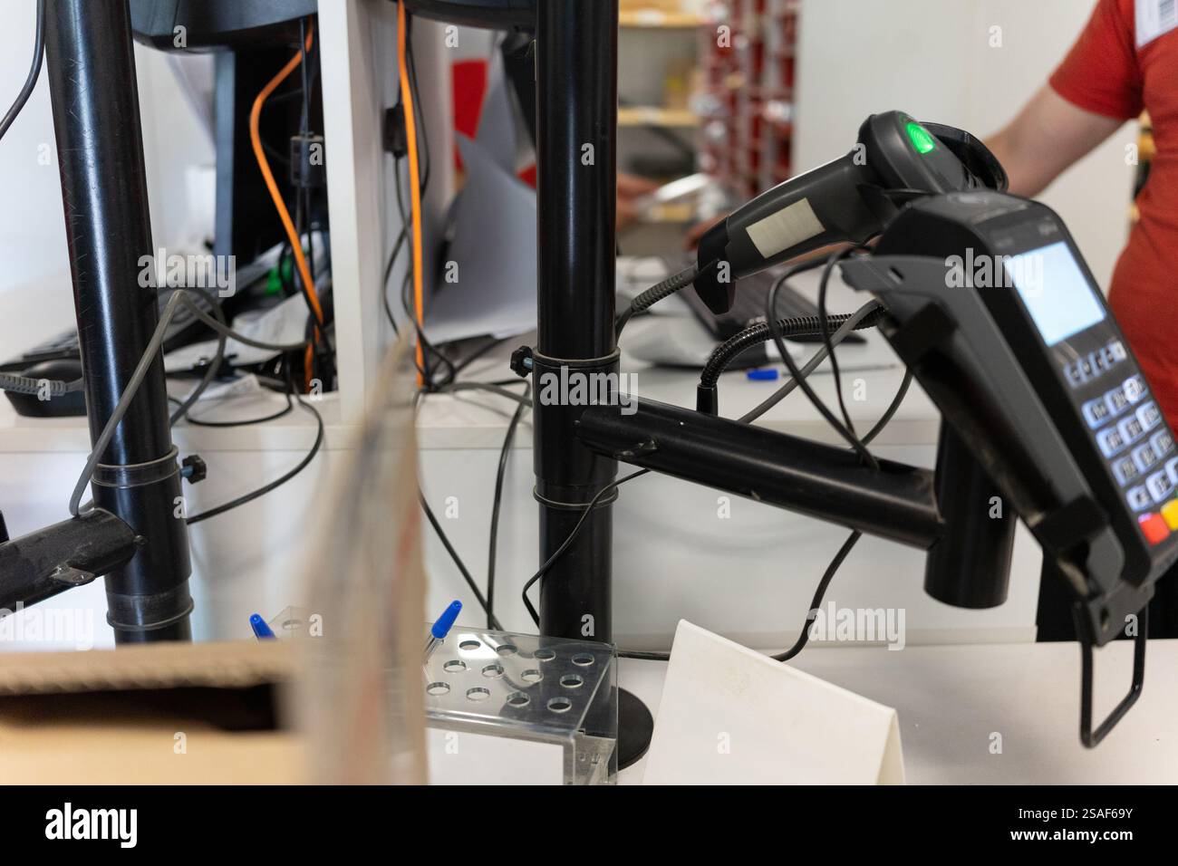 A retail worker stands at the checkout counter, using a scanner to ...