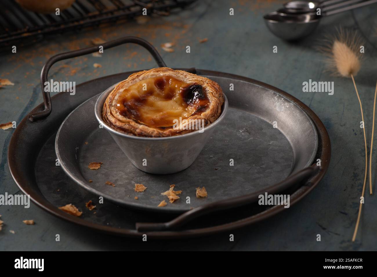 A single Portuguese custard tart in a metal baking tin rests on a round ...