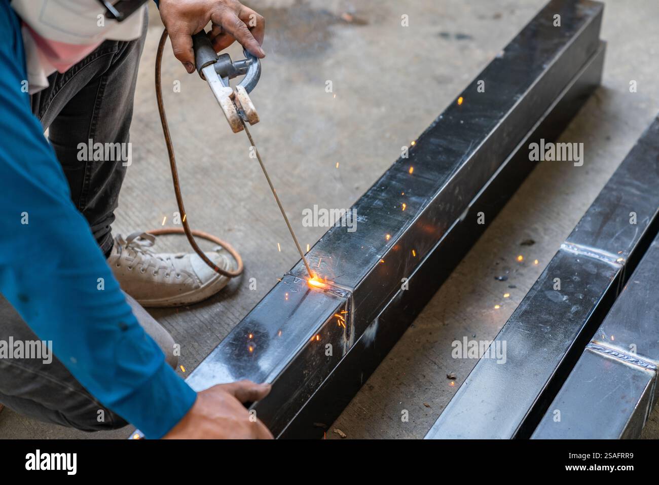 The workers are welding the joint of metal square poles in factory ...