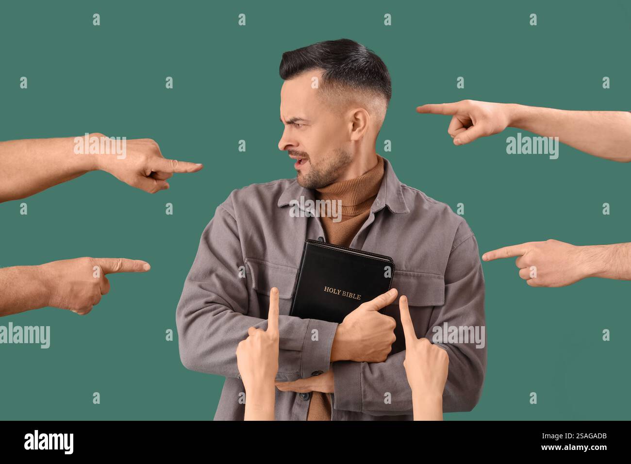 People pointing at young man with Holy Bible on green background ...