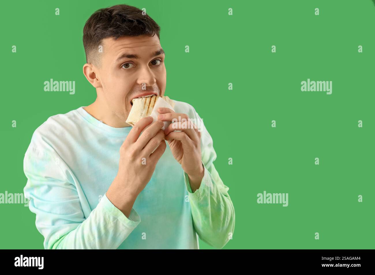 Handsome young man eating tasty doner kebab on green background Stock ...