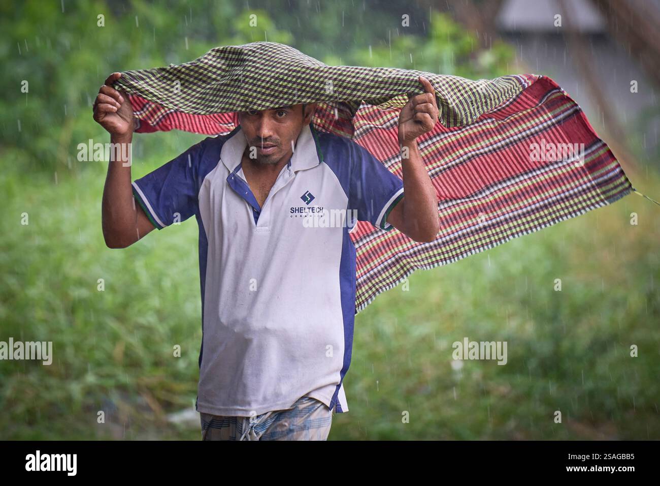 Covering his head under a cloth, a man walks in the rain in Baroigao, a ...