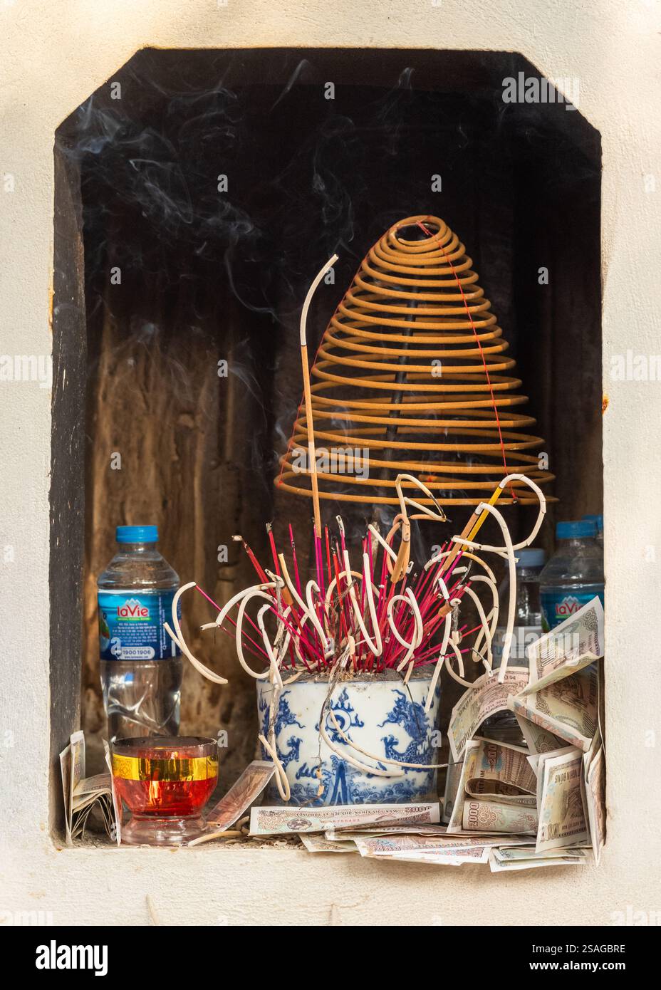 A small shrine with incense, money and other offerings in an alcove on ...