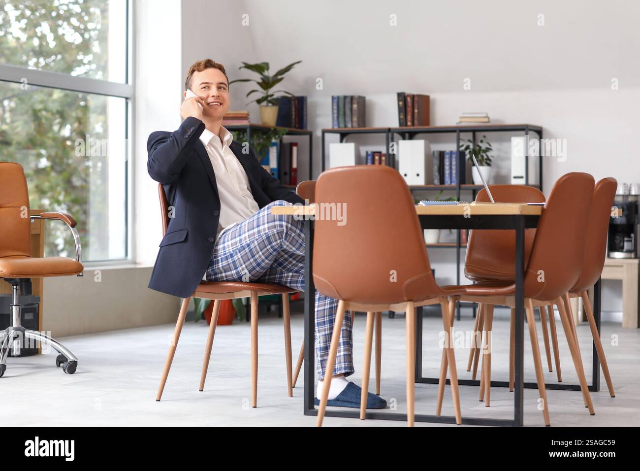 Young businessman talking by mobile phone at table in office. National ...