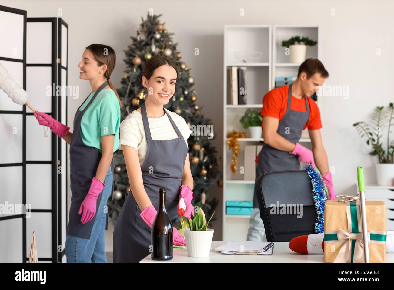Female janitor cleaning table with her team in office after New Year ...
