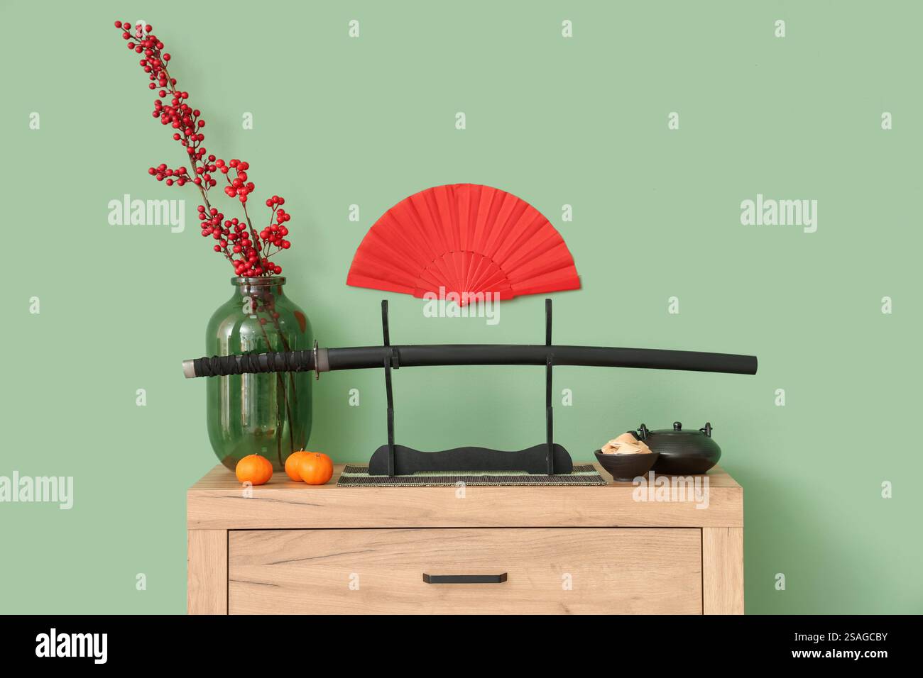 Katana with teapot, Chinese food and vase on commode near green wall ...