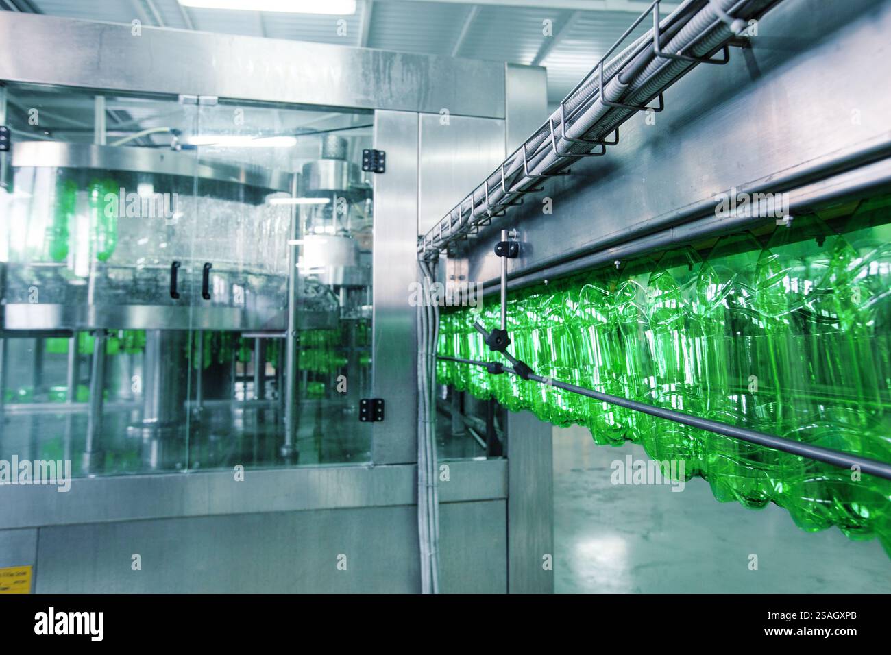 Bottling process in a factory with green plastic bottles moving along a ...