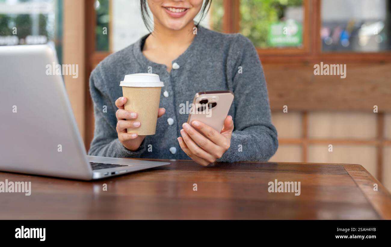 A happy, satisfied Asian woman reads messages on her smartphone and ...