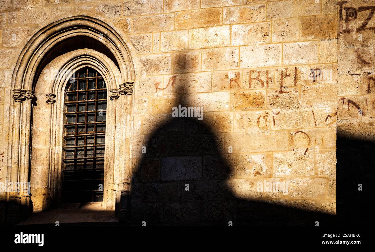 A stone wall with an arched window and intricate details, casting a ...
