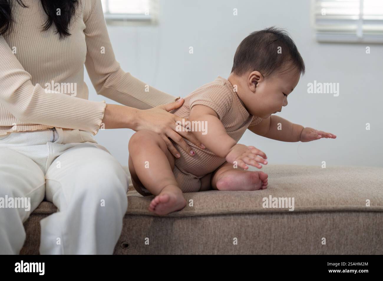 Mother helping baby sit up on a couch, fostering early development and ...