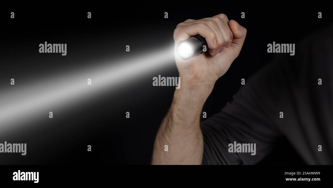 Male hand holding a led flashlight with a wide white beam on a black ...