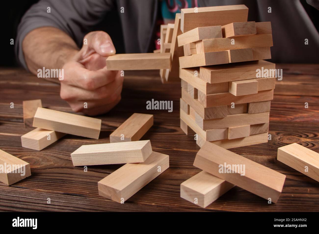 Businessman removing wooden block from falling tower on table ...
