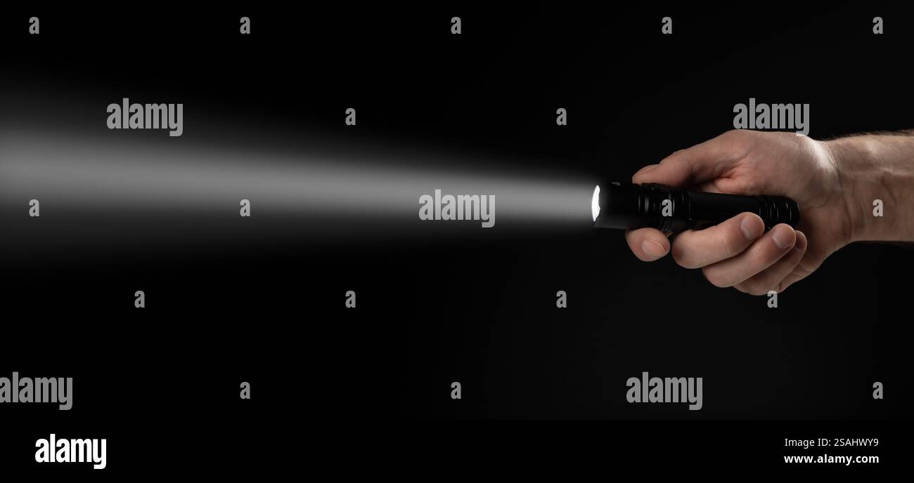 Male hand holding a led flashlight with a wide white beam on a black ...