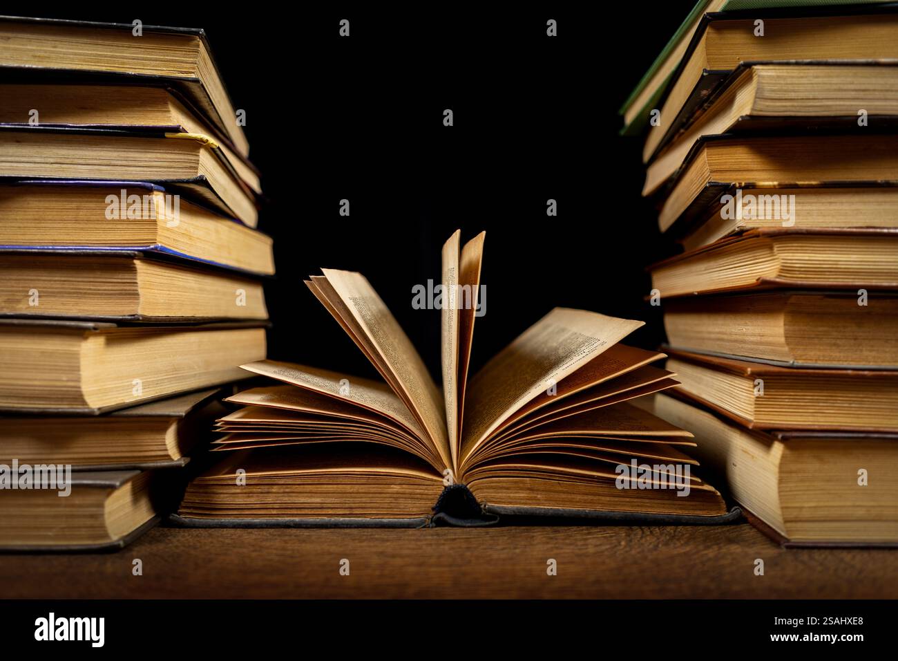 Opened book and stacks of old books on wooden desk in old library ...